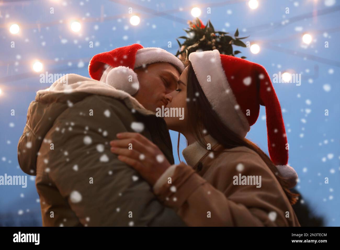 Happy couple kissing under mistletoe bunch outdoors in snowy evening ...