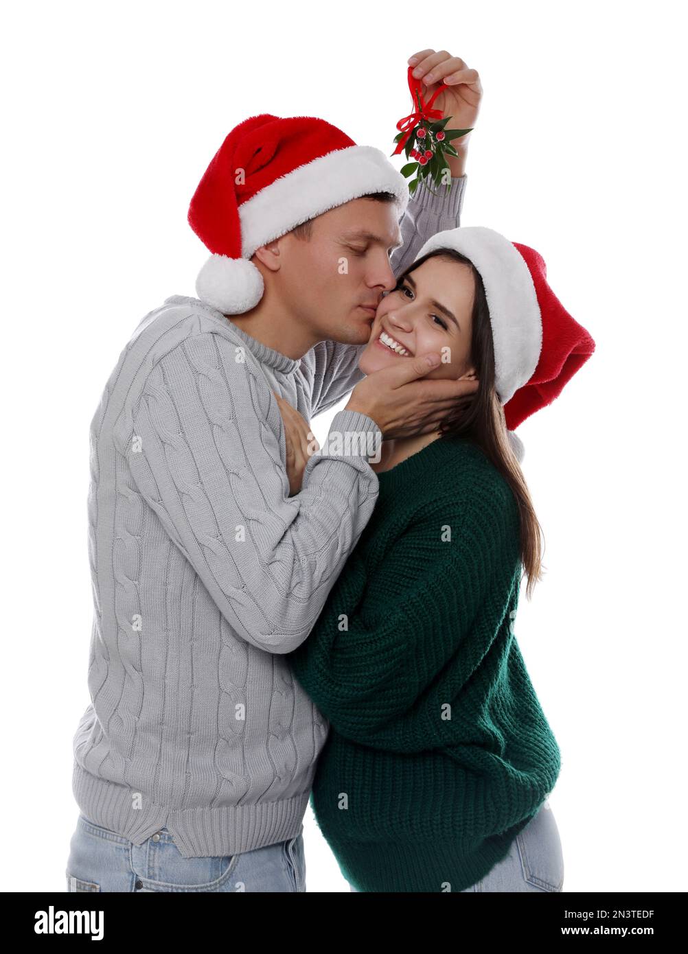 Happy man kissing his girlfriend under mistletoe bunch on white ...