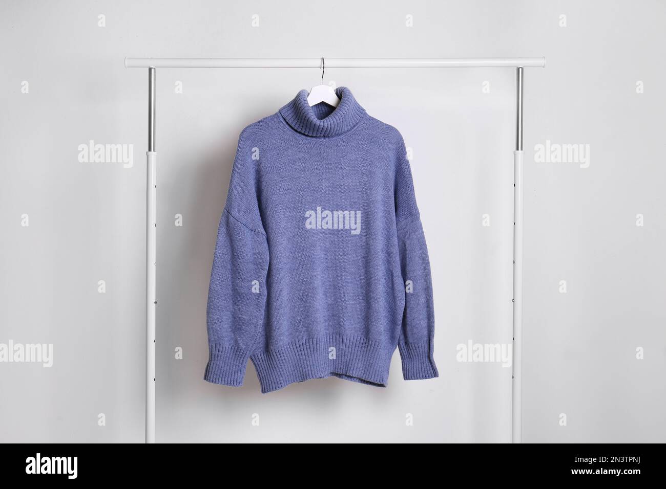 Warm sweater hanging on rack against white background Stock Photo - Alamy