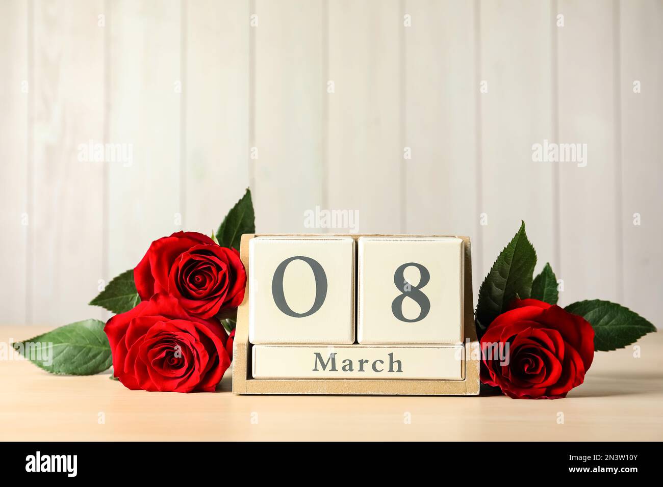 Wooden block calendar with date 8th of March and roses on table against ...