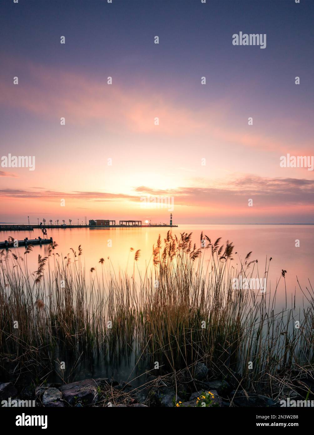 Shore at a lake, with reeds. In the background is a boat landing stage ...