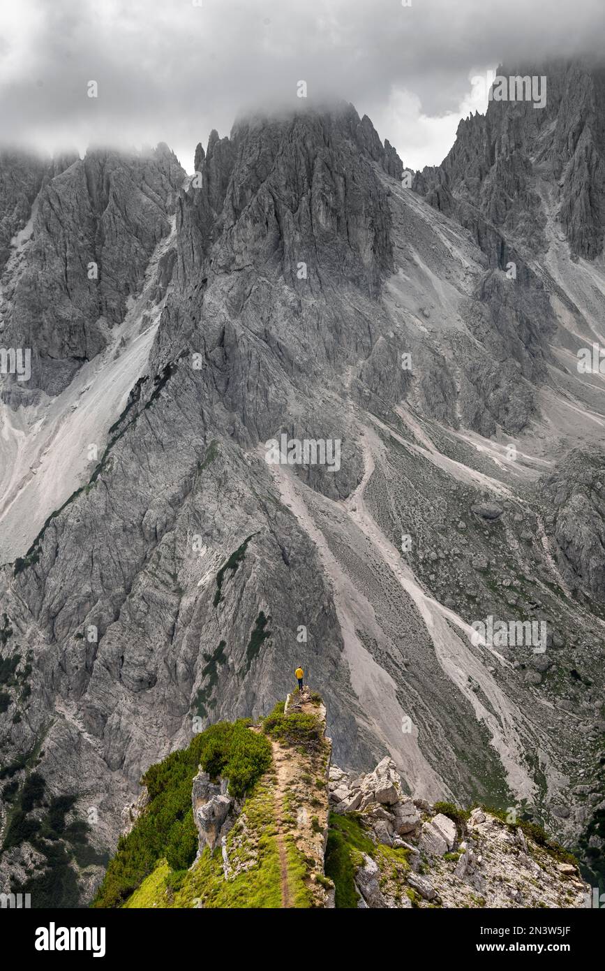 Hiker standing on a ridge, mountain peaks and pointed rocks behind ...