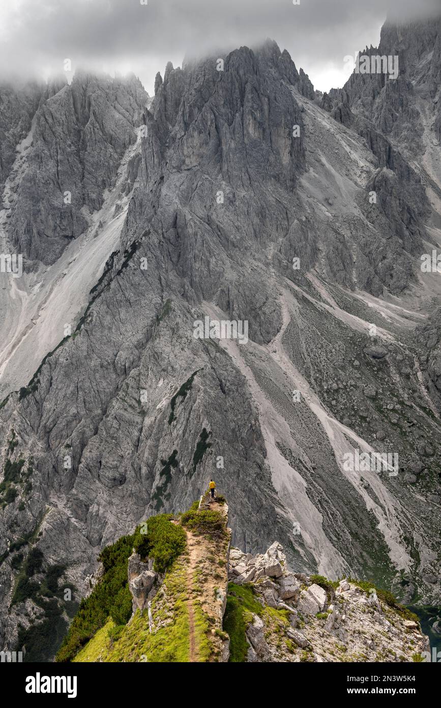 Hiker standing on a ridge, mountain peaks and pointed rocks behind ...
