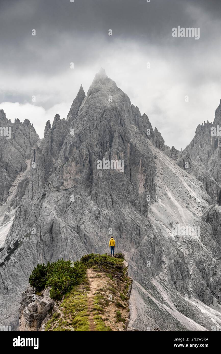 Hiker standing on a ridge, mountain peaks and pointed rocks behind ...
