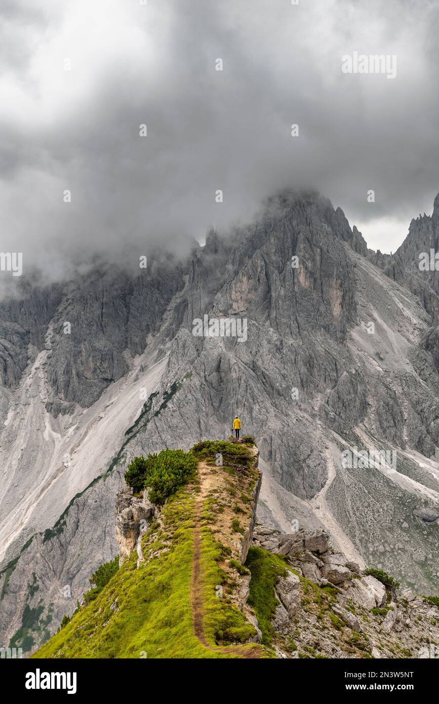 Hiker standing on a ridge, mountain peaks and pointed rocks behind ...
