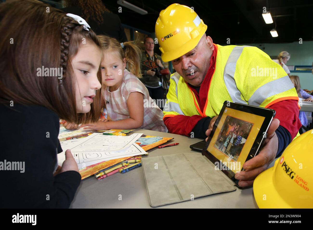 A PSEG Long Island worker looks on as children play with the Let’s Get ...