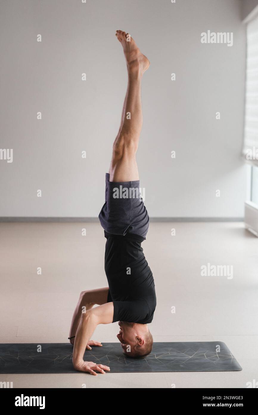 A man performs a yoga pose with support on his head in the gym. Yogi in ...