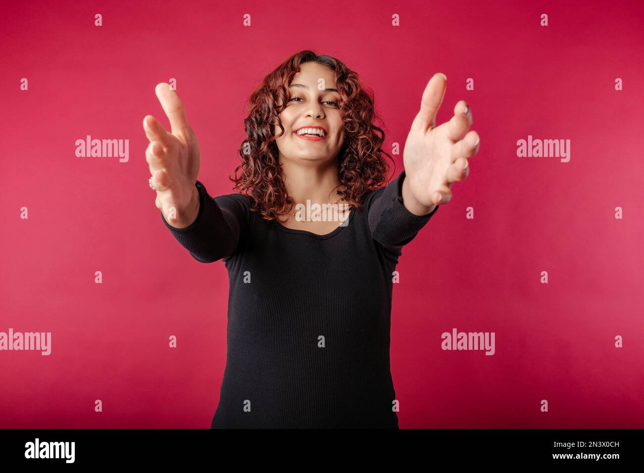 Happy woman wearing black dress standing isolated over red background ...