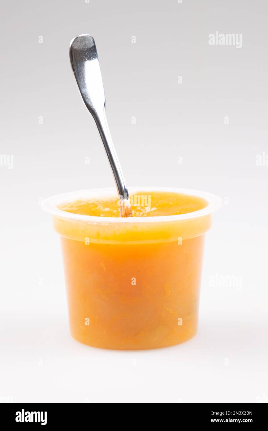plastic peach apricot compote in jar pot close with spoon on white ...