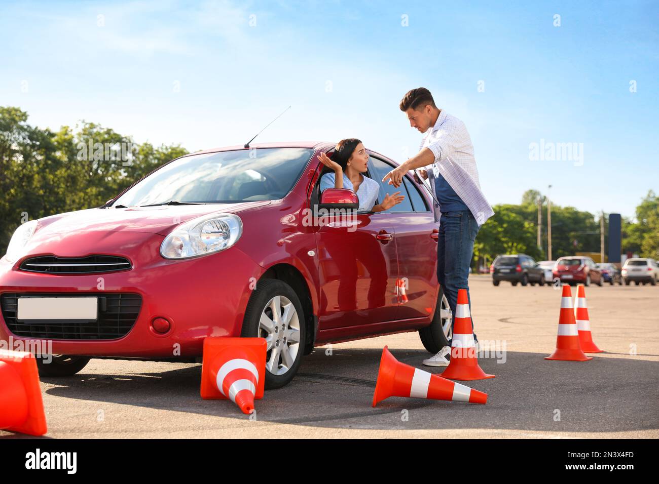 Stressed young woman in car near instructor and fallen traffic cones ...