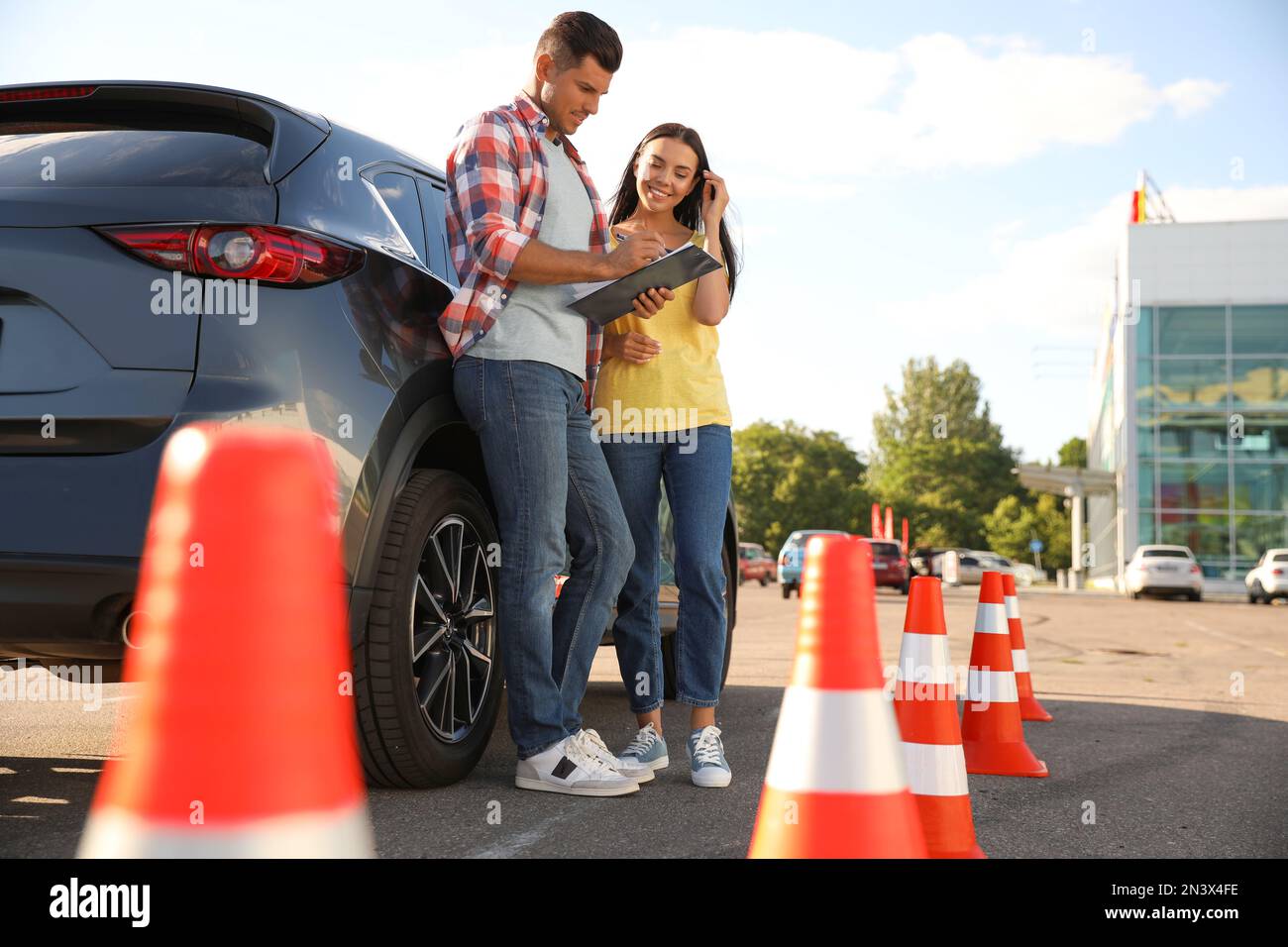 Instructor with clipboard and his student near car outdoors. Driving ...