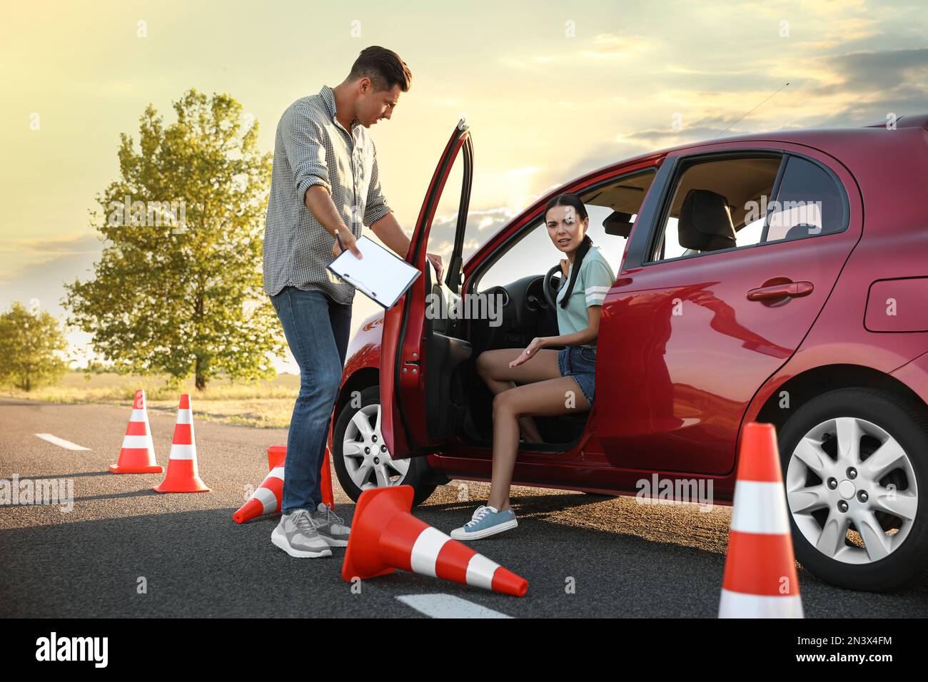 Stressed young woman in car near instructor and fallen traffic cones ...