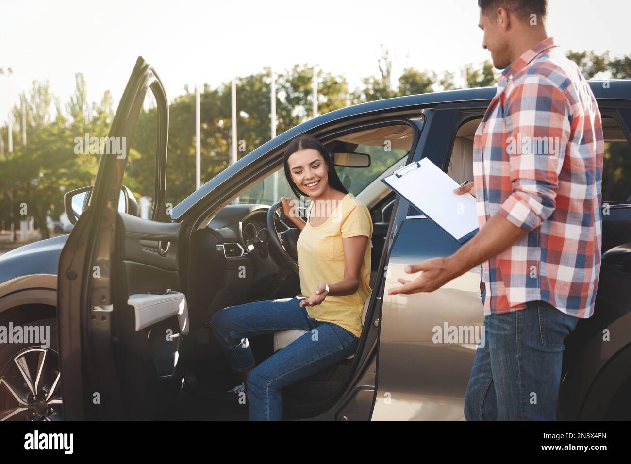 Instructor with clipboard and his student near car outdoors. Driving ...