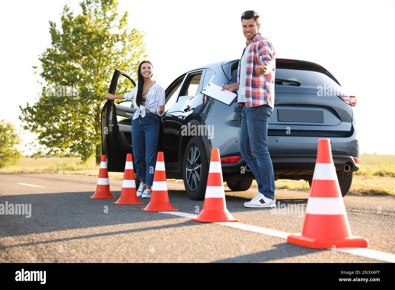 Instructor with clipboard and his student near car outdoors. Driving ...