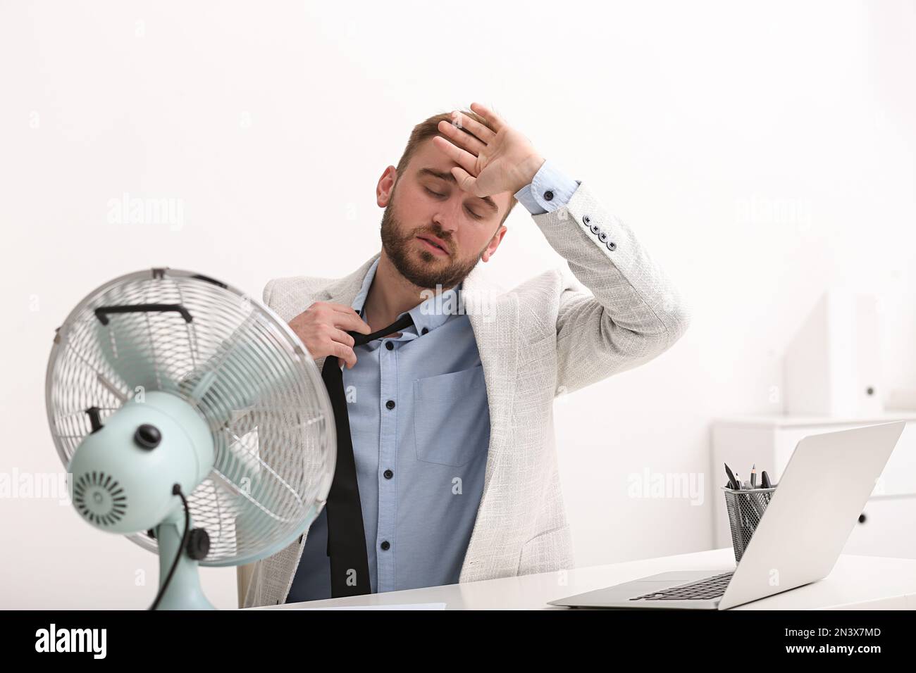 Man suffering from heat in front of fan at workplace Stock Photo - Alamy