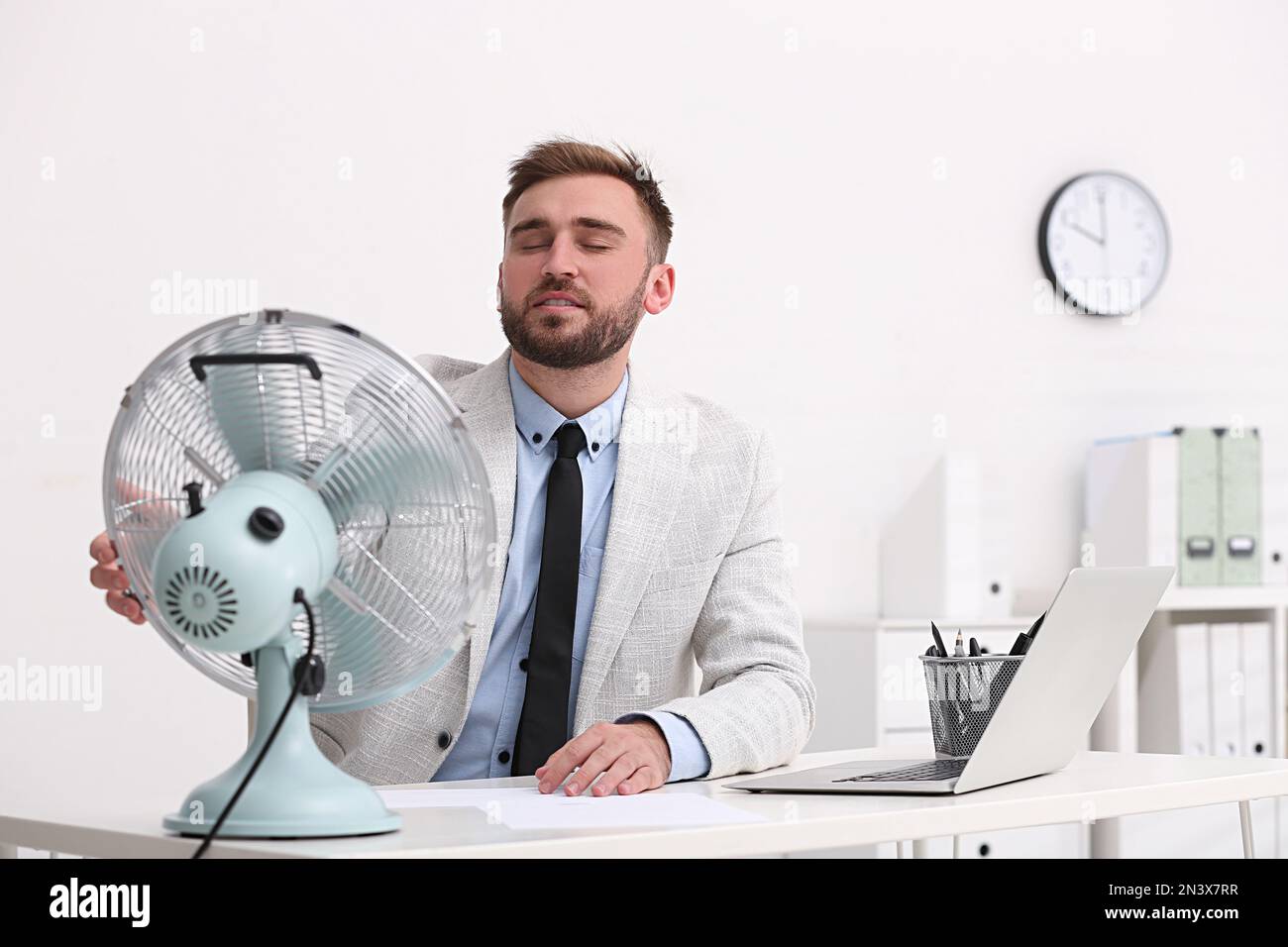 Man enjoying air flow from fan at workplace Stock Photo - Alamy