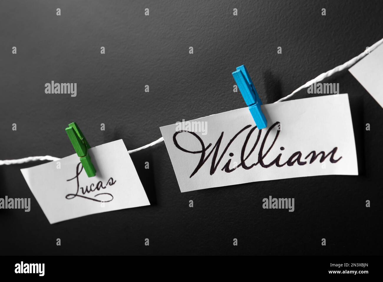Paper pieces with baby names on rope against black background, closeup ...