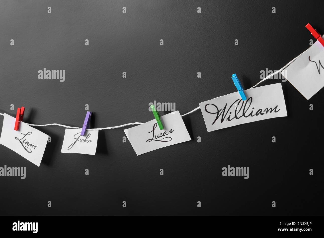 Paper pieces with baby names on rope against black background, closeup ...