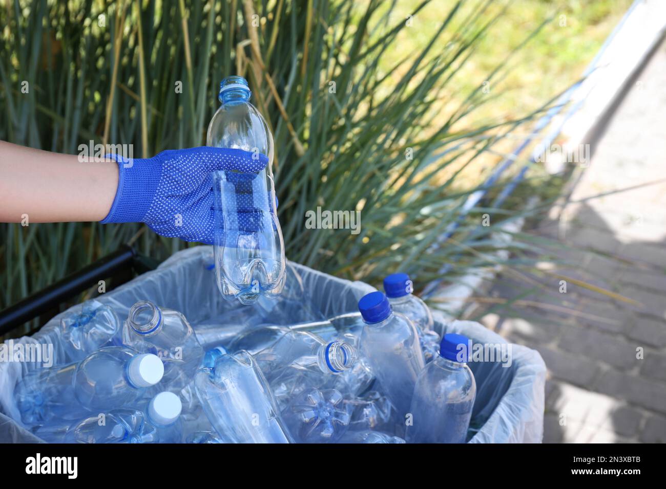 Woman in gloves putting used plastic bottle into trash bin outdoors ...