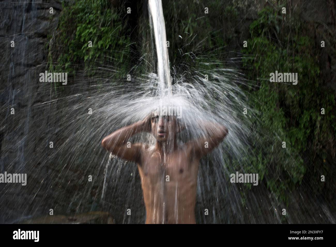 A Pakistani worker takes a shower under a water supply pipe, following ...