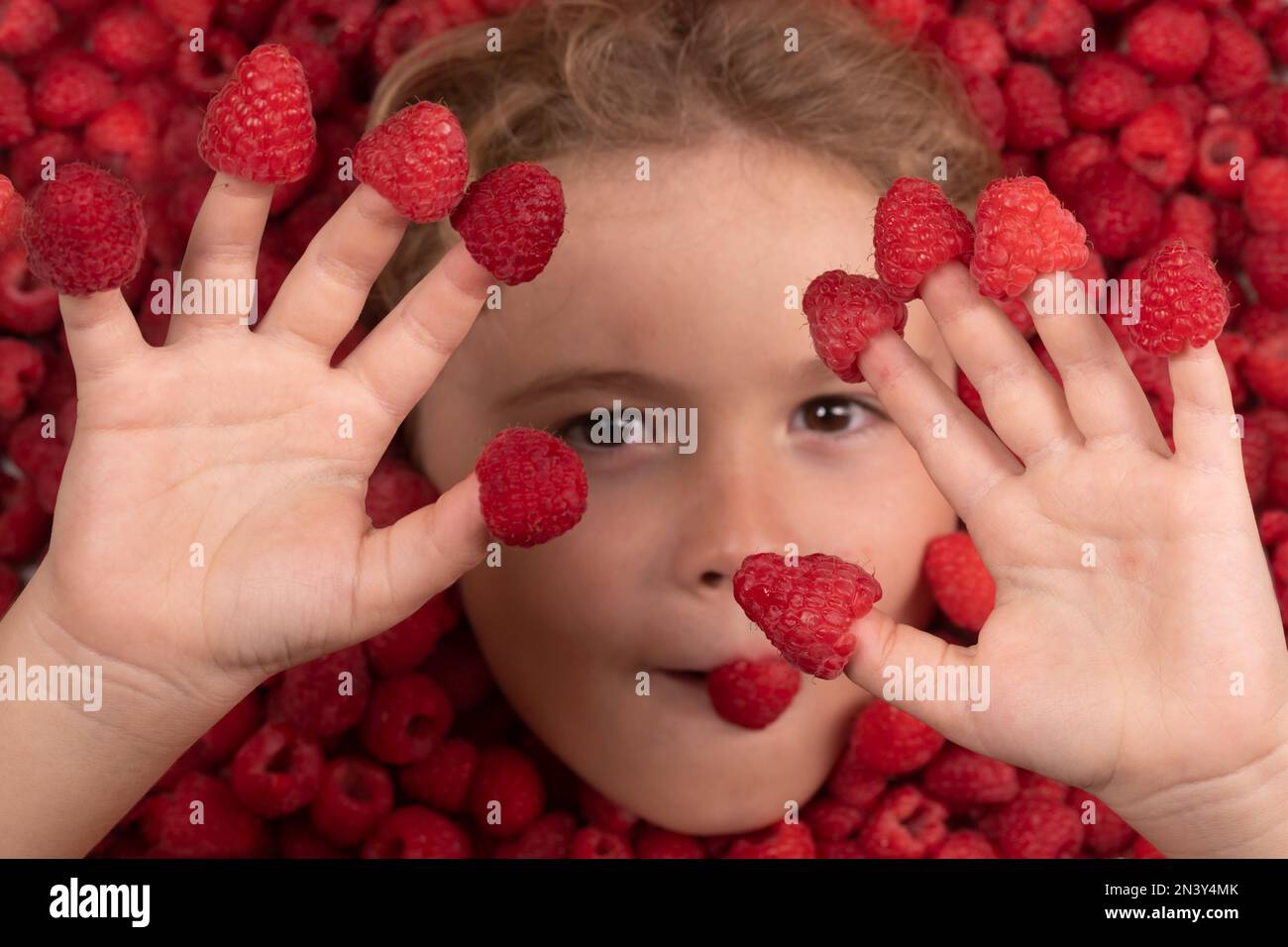 Summer fruits. Top view photo of child face in raspberries background ...