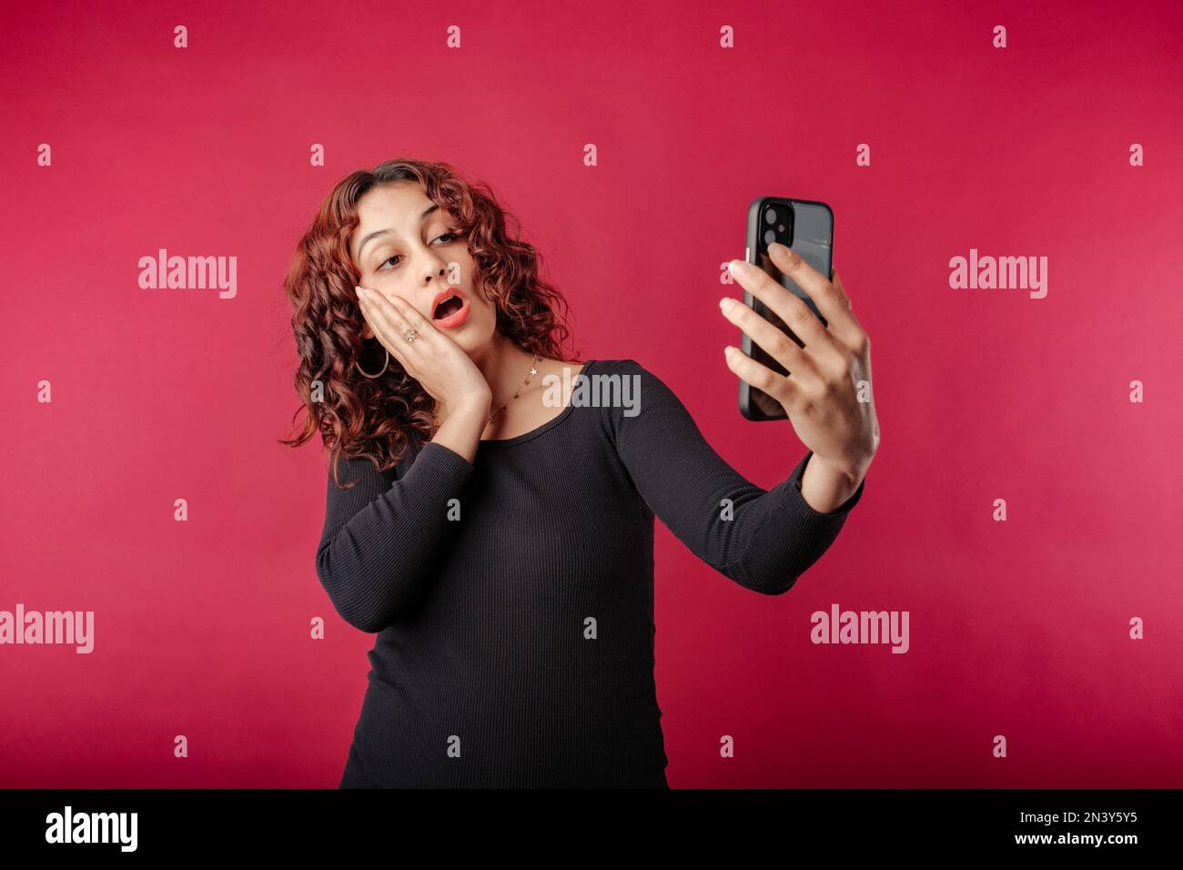 Young beautiful woman wearing black ribbed dress isolated over red ...
