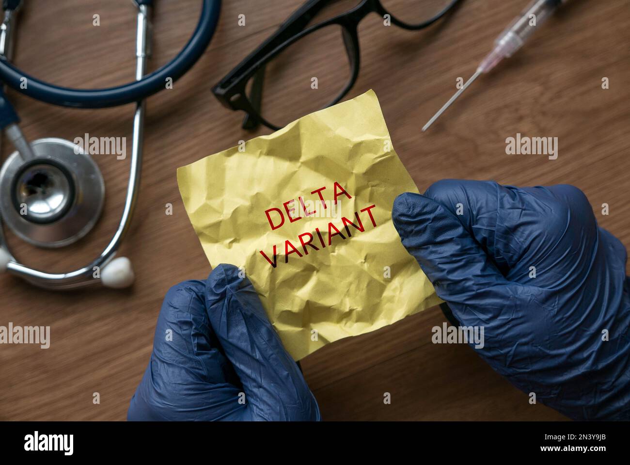 A hand wearing blue glove opening a crumpled yellow memo note written ...