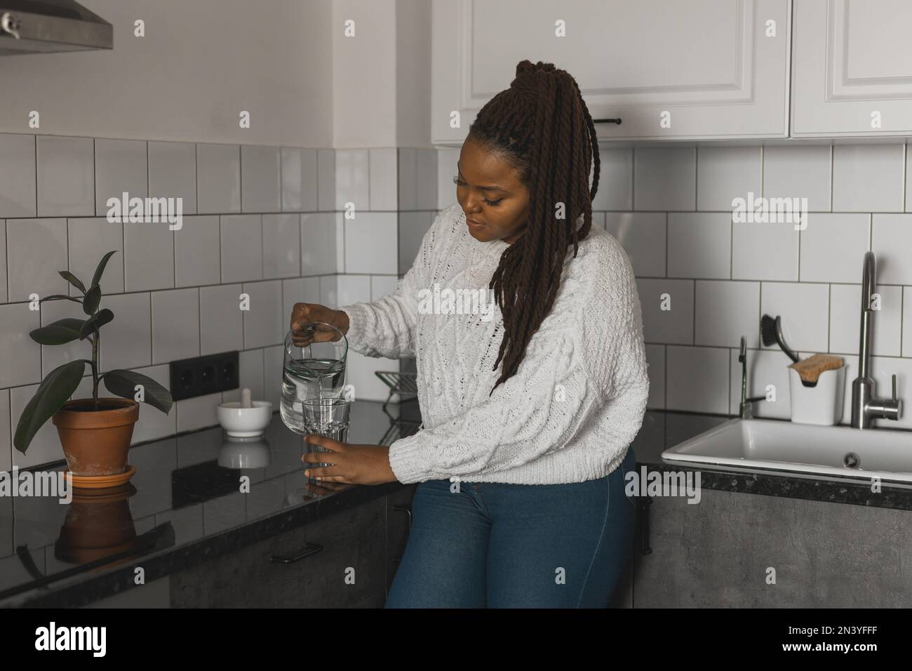 Thirsty african american woman drinking mineral water in kitchen ...