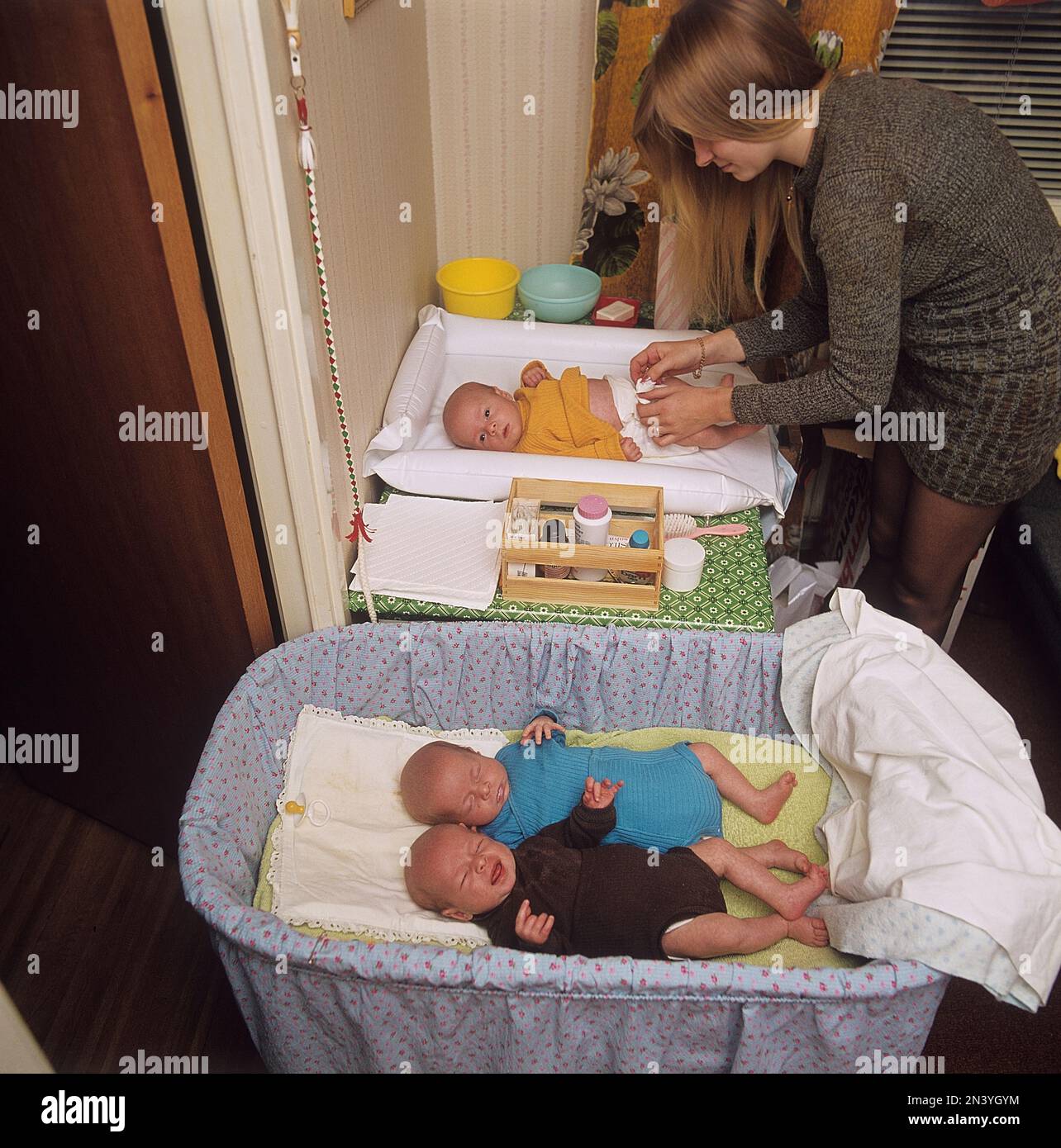 1970s mother. A woman is cleaning and changing diapers on of her three ...