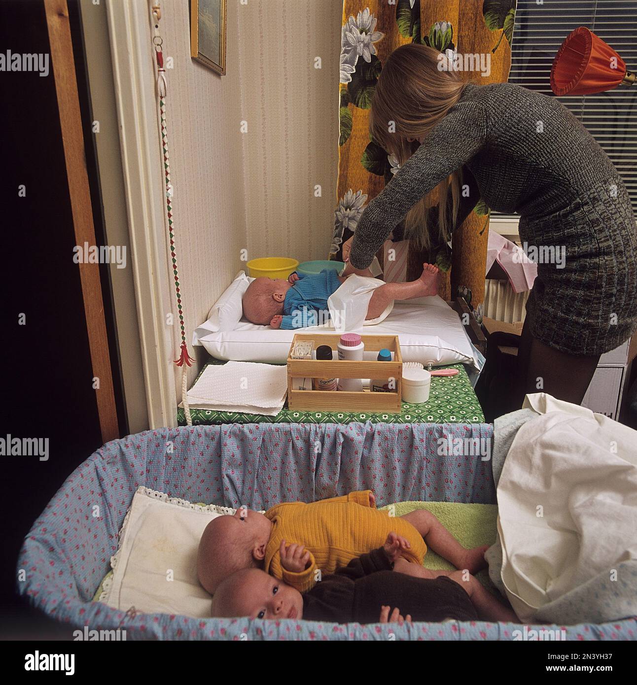 1970s mother. A woman is cleaning and changing diapers on of her three ...