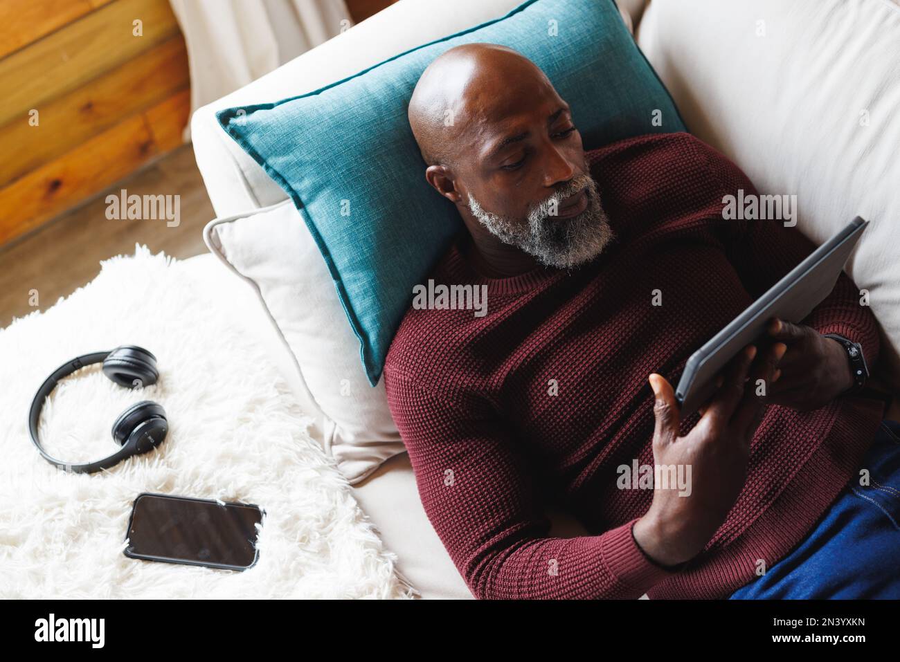 Bald african american senior man using tablet while lying on sofa in log cabin Stock Photo - Alamy
