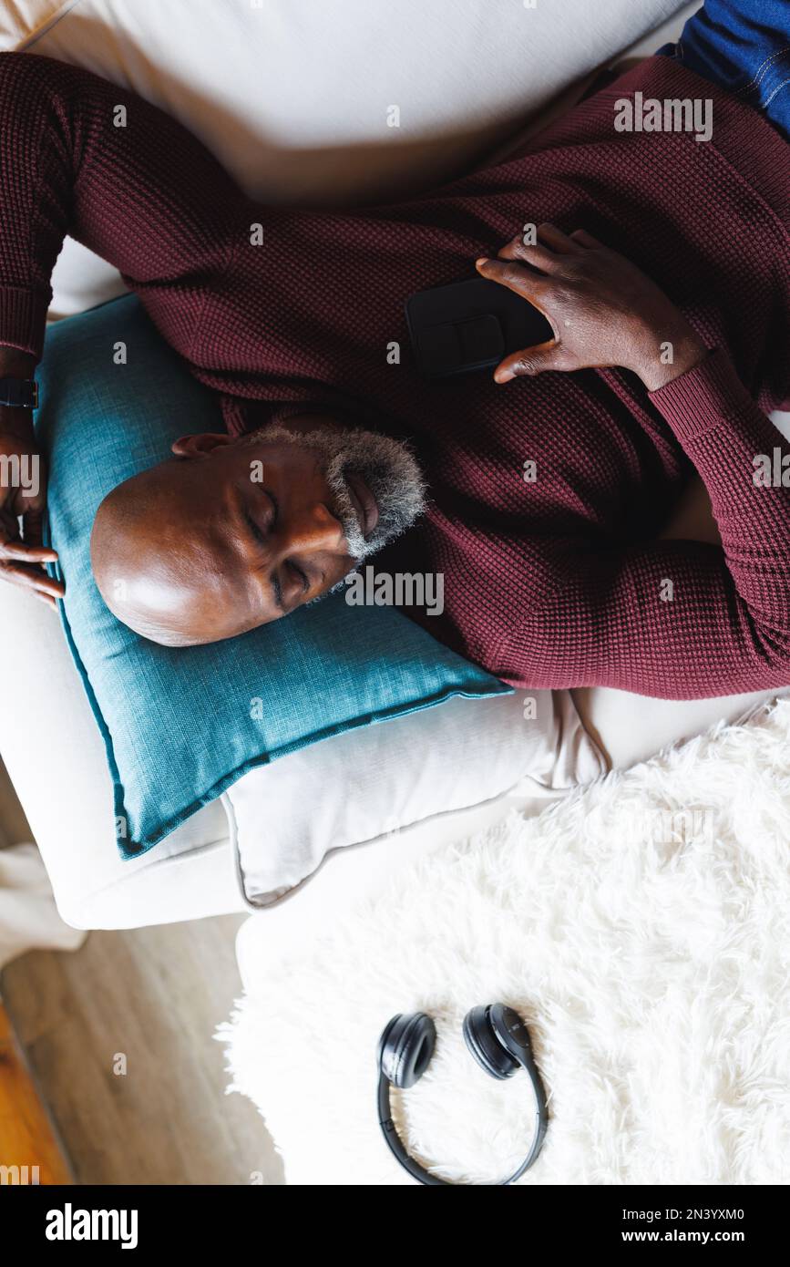 Overhead view of bald african american senior man with mobile phone sleeping on couch at log ...