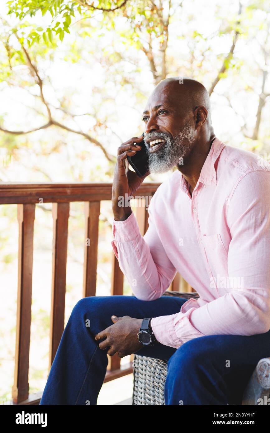 Bald african american senior man talking over mobile phone while sitting in balcony at log cabin ...
