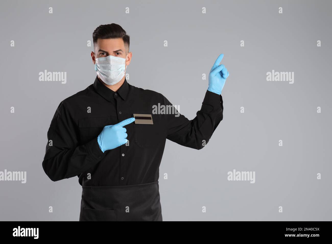Waiter wearing medical face mask on light grey background Stock Photo ...