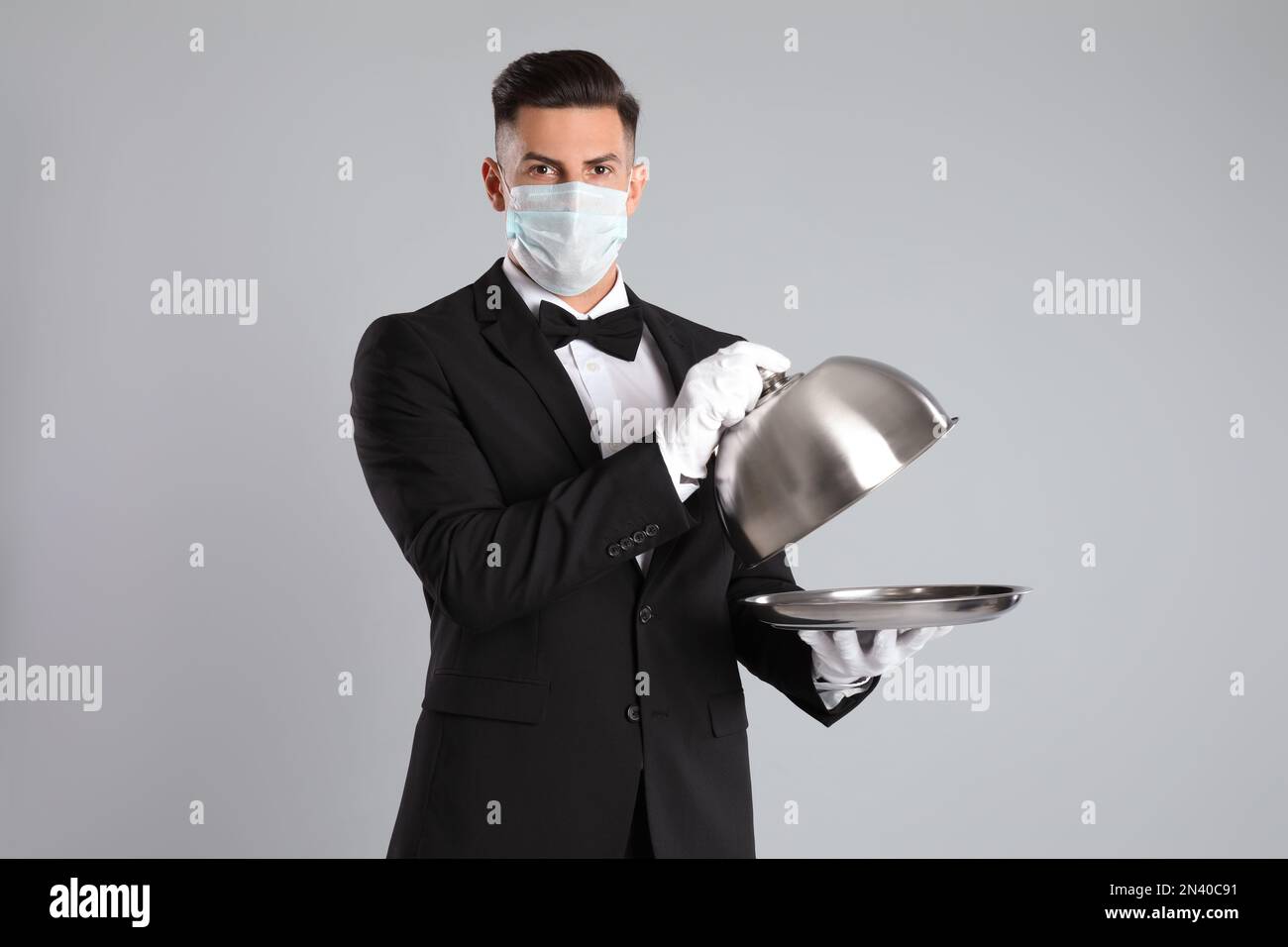 Waiter in medical face mask with empty tray on light grey background ...
