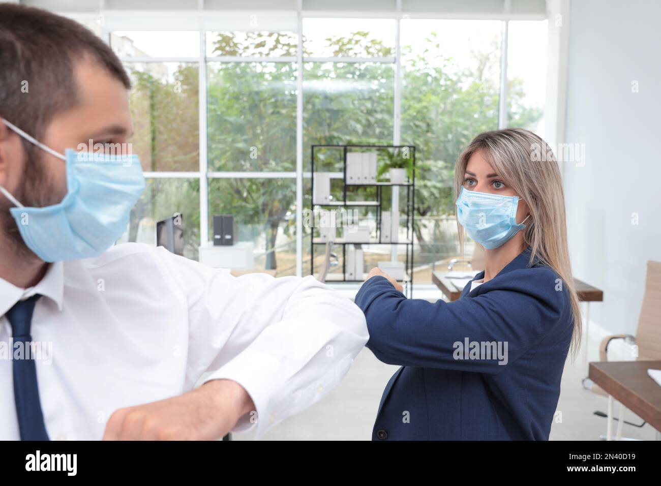 Office employees in masks greeting each other by bumping elbows at ...