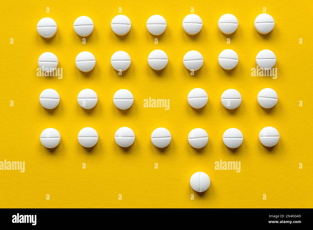 A row of white medical pills on yellow background with one missing spot ...