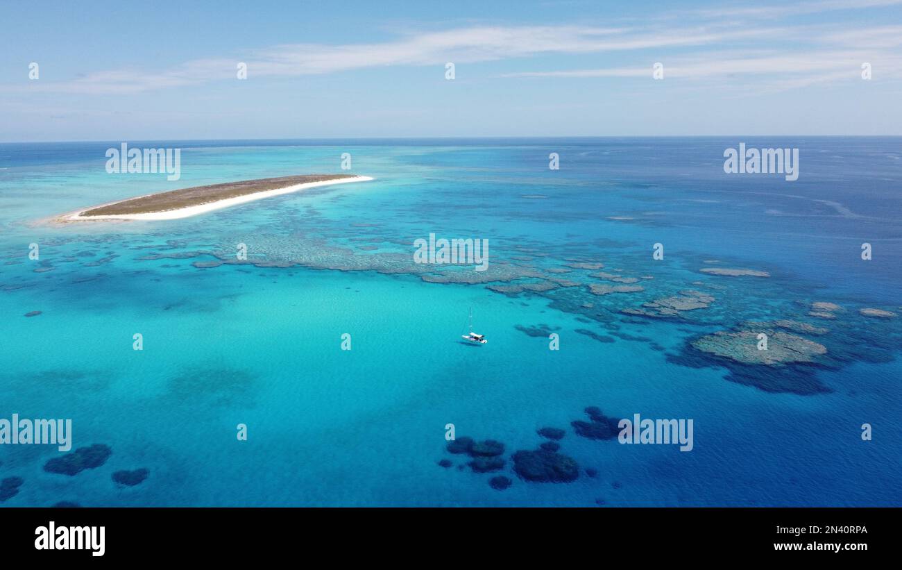 Aerial shot of sailing boat anchored in a clear lagoon with a tropical ...
