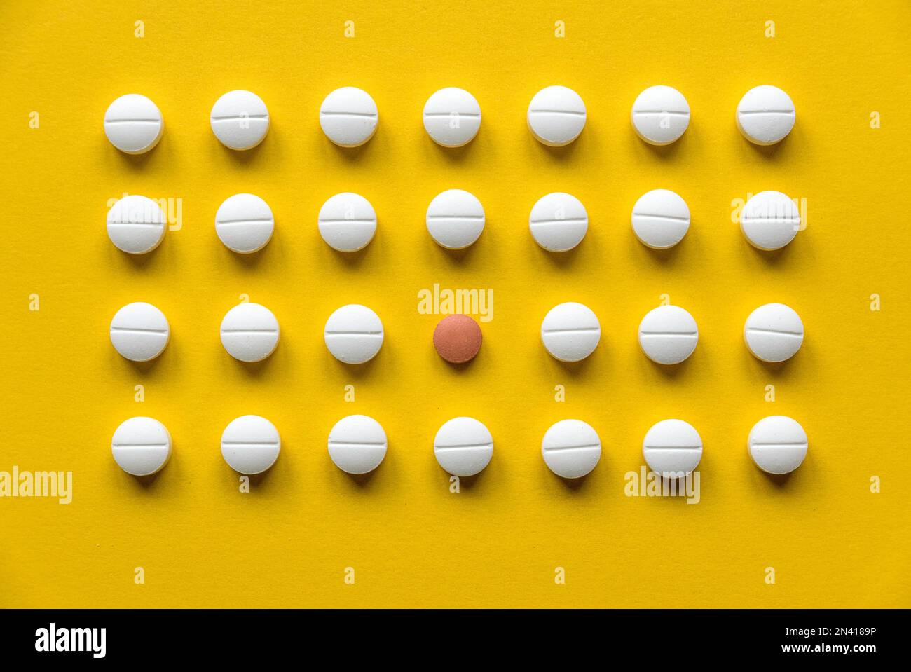 A row of white medical pills and one red pill in the middle on yellow ...