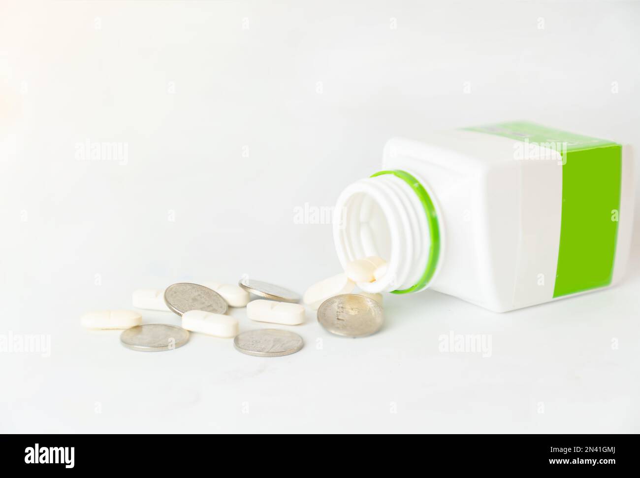 Pills and coins falling from bottle on white background concept of ...
