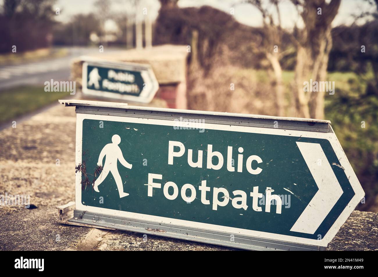 Public footpath signs attached to low wall by the side of an A road in ...