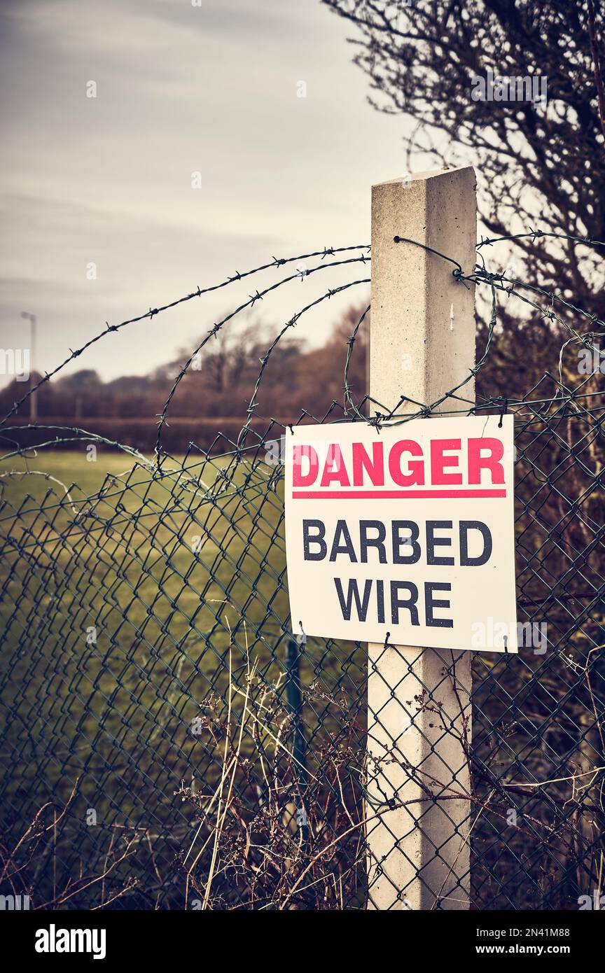 Sign warning of barbed wire attached to wire fence Stock Photo - Alamy