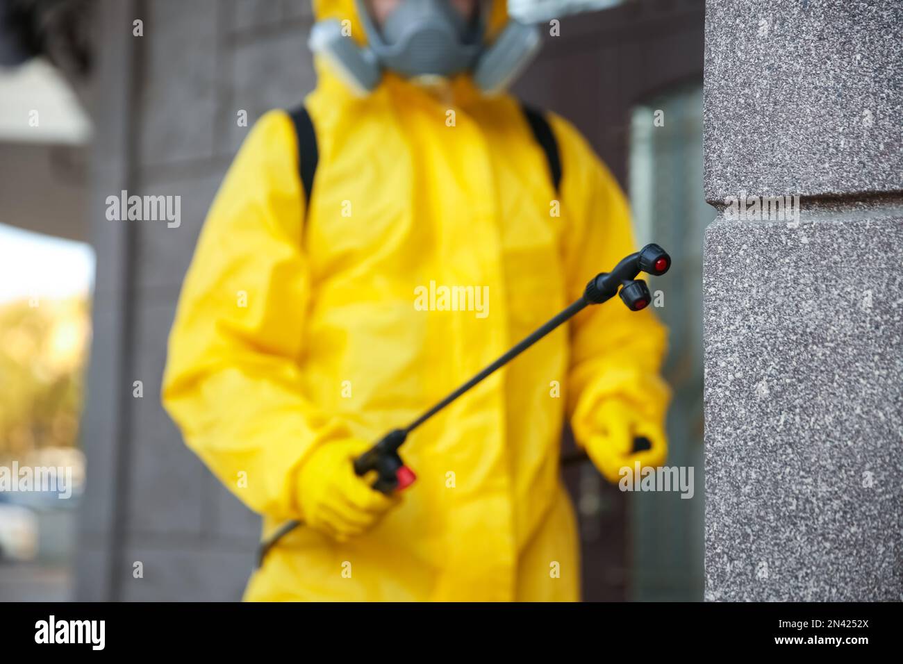 Person in hazmat suit disinfecting building wall outdoors, focus on ...