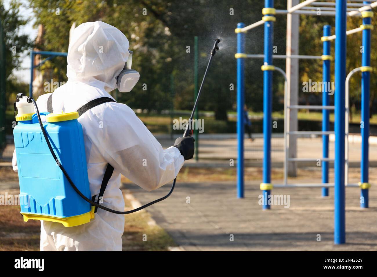 Person in hazmat suit spraying disinfectant around outdoor gym. Surface ...