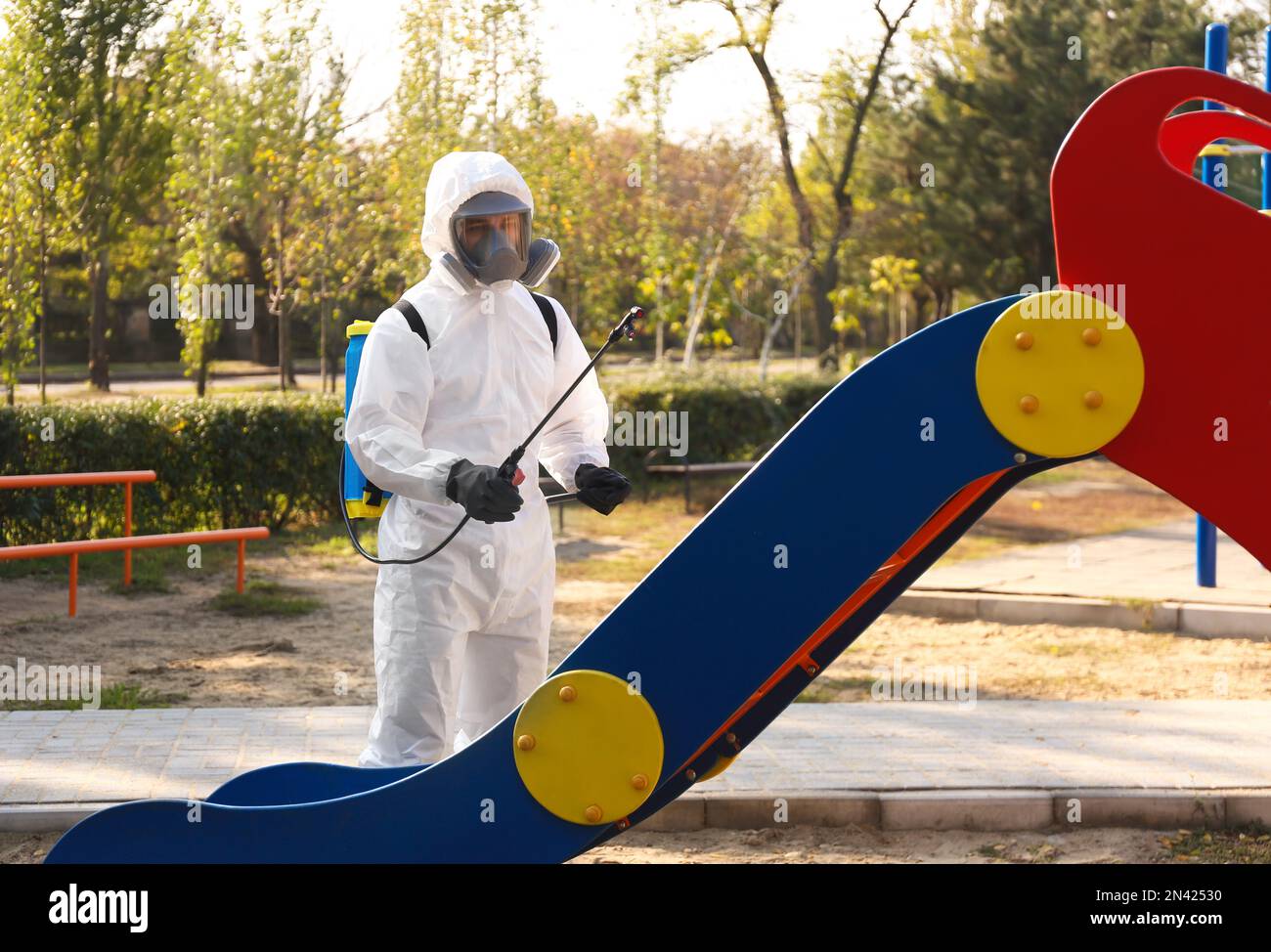Man in hazmat suit with disinfectant sprayer near slide at children's ...