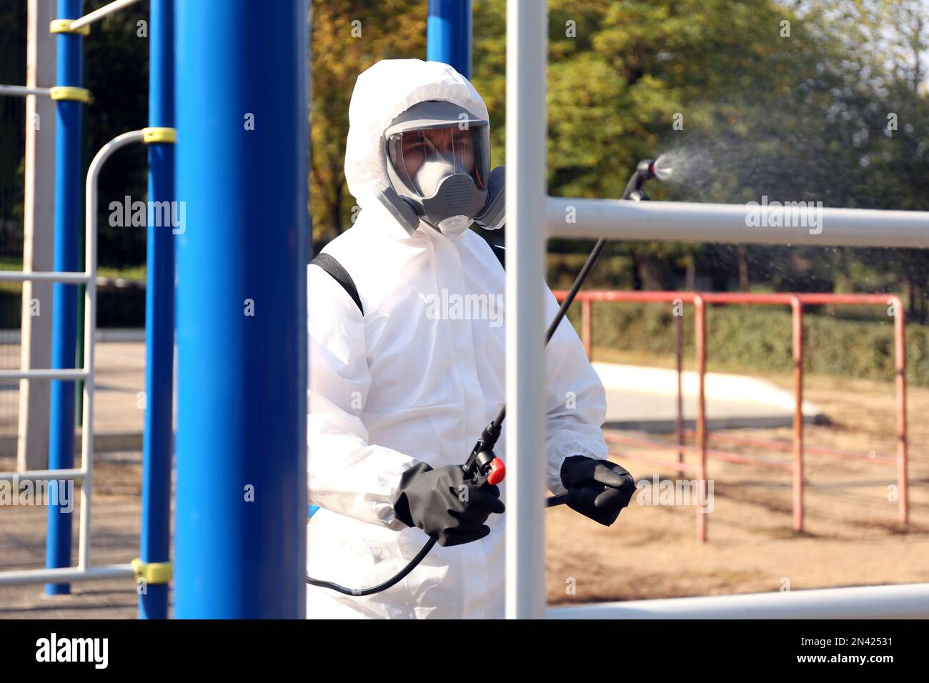 Man in hazmat suit spraying disinfectant on outdoor gym's equipment ...