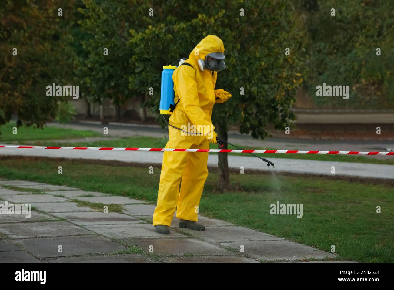 Person in hazmat suit disinfecting street pavement with sprayer ...