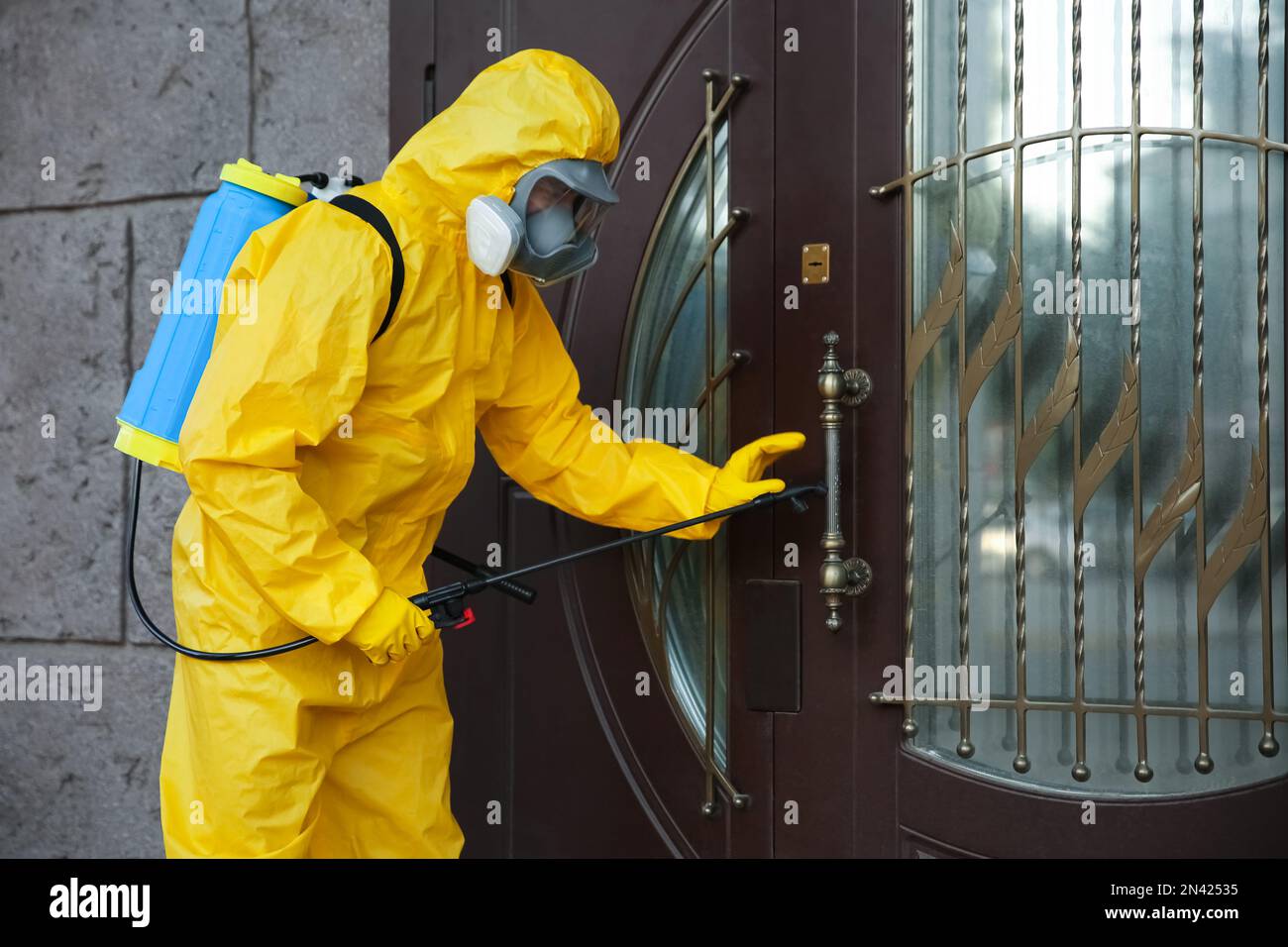 Person in hazmat suit disinfecting entrance door with sprayer. Surface ...
