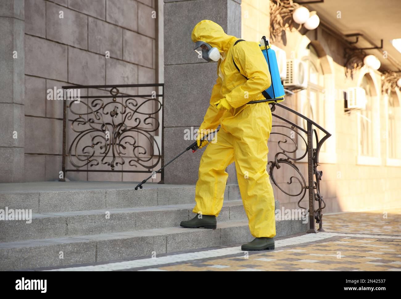 Person in hazmat suit disinfecting stairs with sprayer outdoors ...
