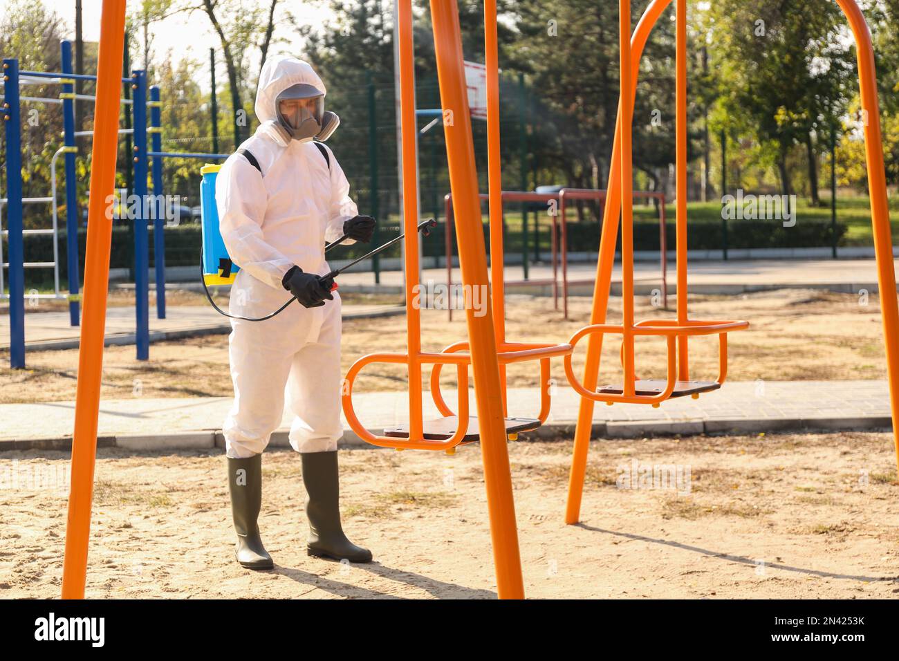 Man in hazmat suit with disinfectant sprayer near swing at children's ...